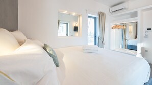 Quarto de hotel com uma cama grande, uma janela pequena, um ar condicionado e um espelho.