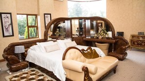Um quarto luxuoso com uma cama grande, um chaise longue, uma toucador com espelho e uma cômoda.
