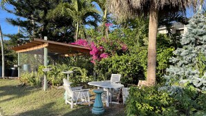 Pátio com mesa e cadeiras, cercado por vegetação exuberante e plantas floridas.