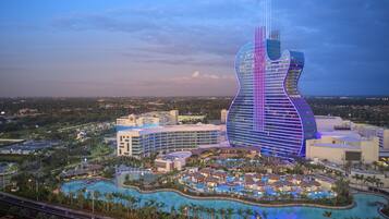 Um hotel com um edifício em formato de guitarra, uma piscina grande e vegetação ao redor.