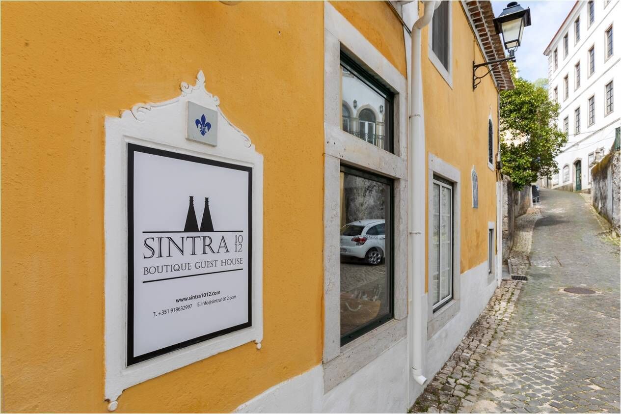 Uma residência de hóspedes boutique chamada SINTRA 19, com uma placa, uma janela com vista para um carro estacionado e uma rua de calçada portuguesa.