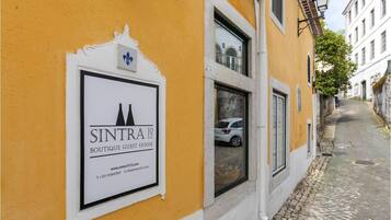 Uma residência de hóspedes boutique chamada SINTRA 19, com uma placa, uma janela com vista para um carro estacionado e uma rua de calçada portuguesa.