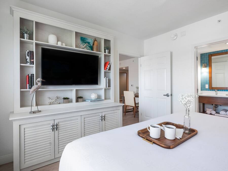 Quarto de hotel com cama grande, televisão montada, área de refeições e banheiro com espelho e porta-toalhas.