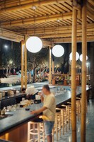 Uma área de bar com colunas de bambu, mesas redondas e banquetas.