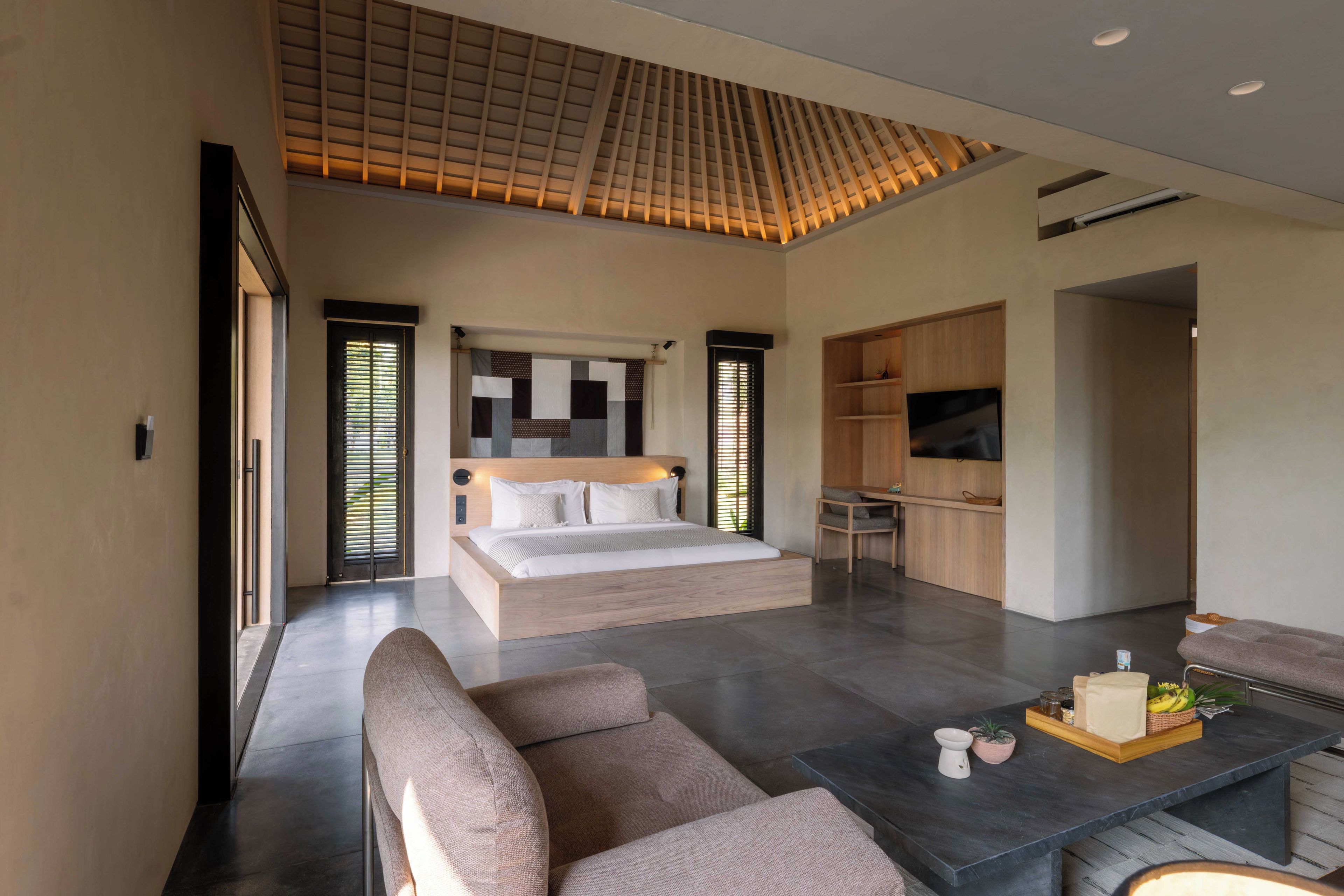 Quarto moderno com cama grande, sofá, televisão e área de jantar.