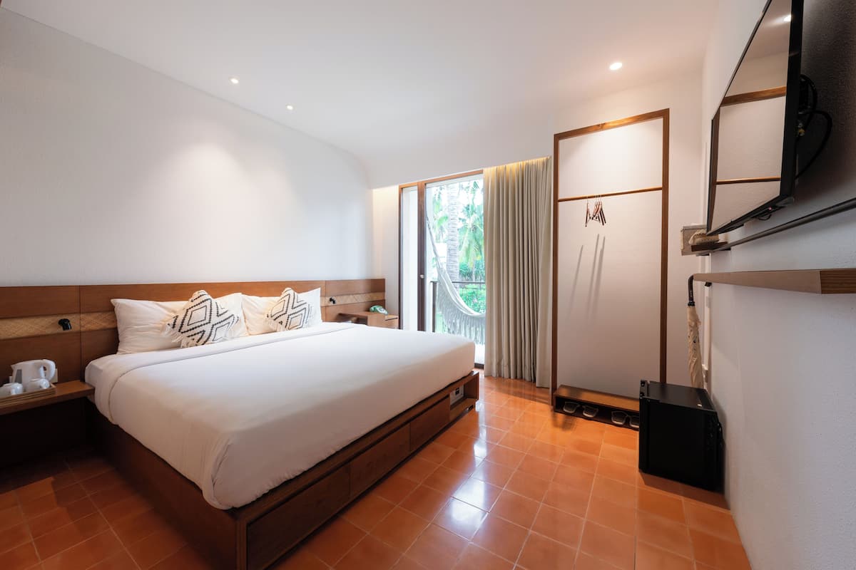 Quarto de hotel com uma cama grande, televisão, guarda-roupa e varanda com cortinas.