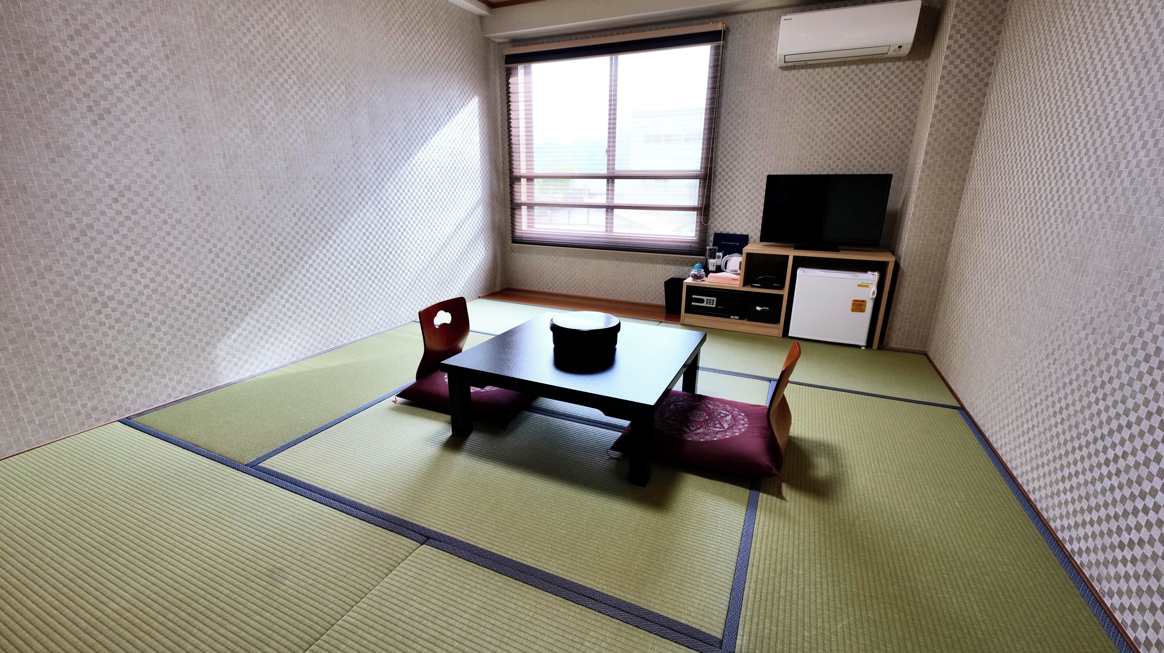 Um quarto com esteiras de tatame, uma mesa baixa, duas cadeiras, uma televisão e um frigorífico.