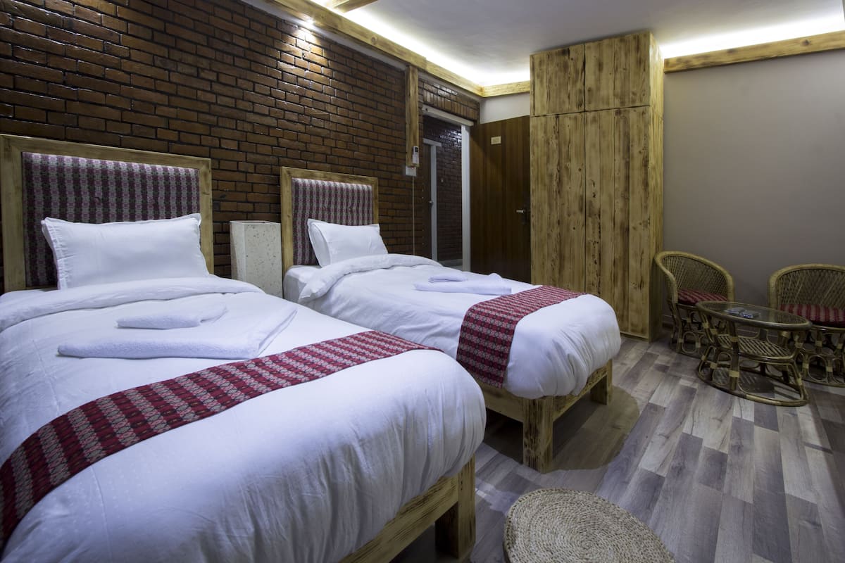 Quarto de hotel com duas camas, um guarda-roupa de madeira, uma mesa redonda pequena e cadeiras de vime.