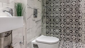 Uma casa de banho moderna com lavatório de mármore, sanita e chuveiro com azulejos estampados.