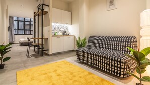 Sala moderna com um sofá estampado, um tapete amarelo e uma área de cozinha com painel de fundo padronizado.