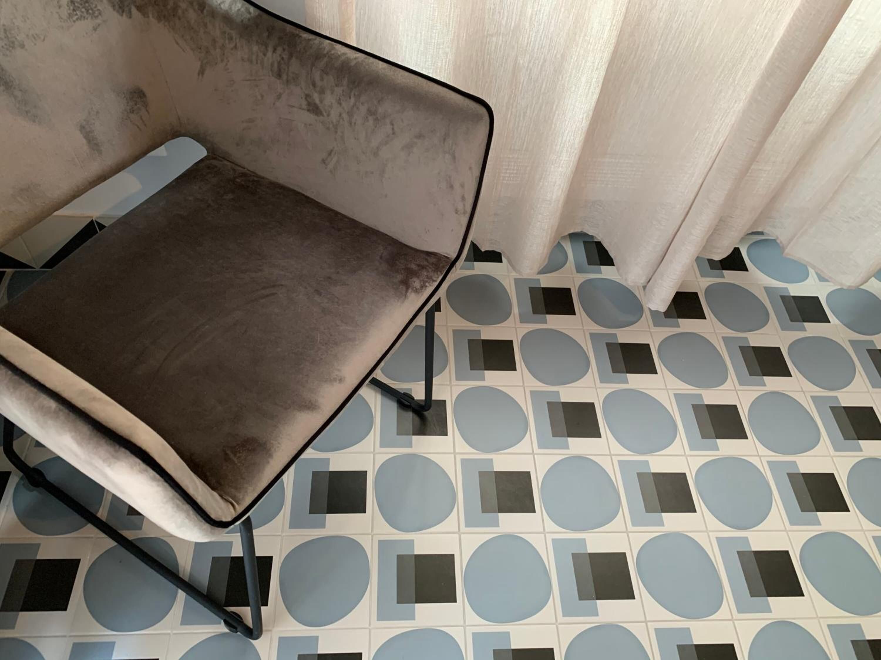 Uma cadeira com almofada escura e estrutura metálica, sobre um piso com padrão geométrico de azulejos.