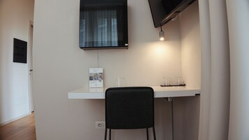 Quarto pequeno e moderno, com escrivaninha, cadeira e televisão na parede.