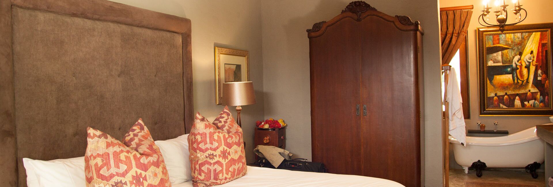 Quarto com uma cama grande, um guarda-roupa de madeira, uma mesa de cabeceira com abajur e um quadro na parede.