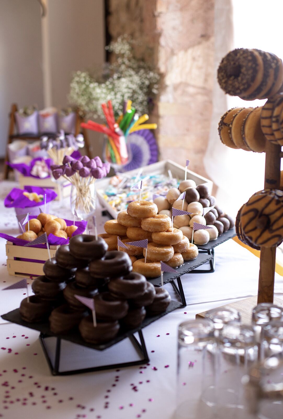 Uma mesa com diversos alimentos, incluindo donuts e doces, dispostos em suportes.