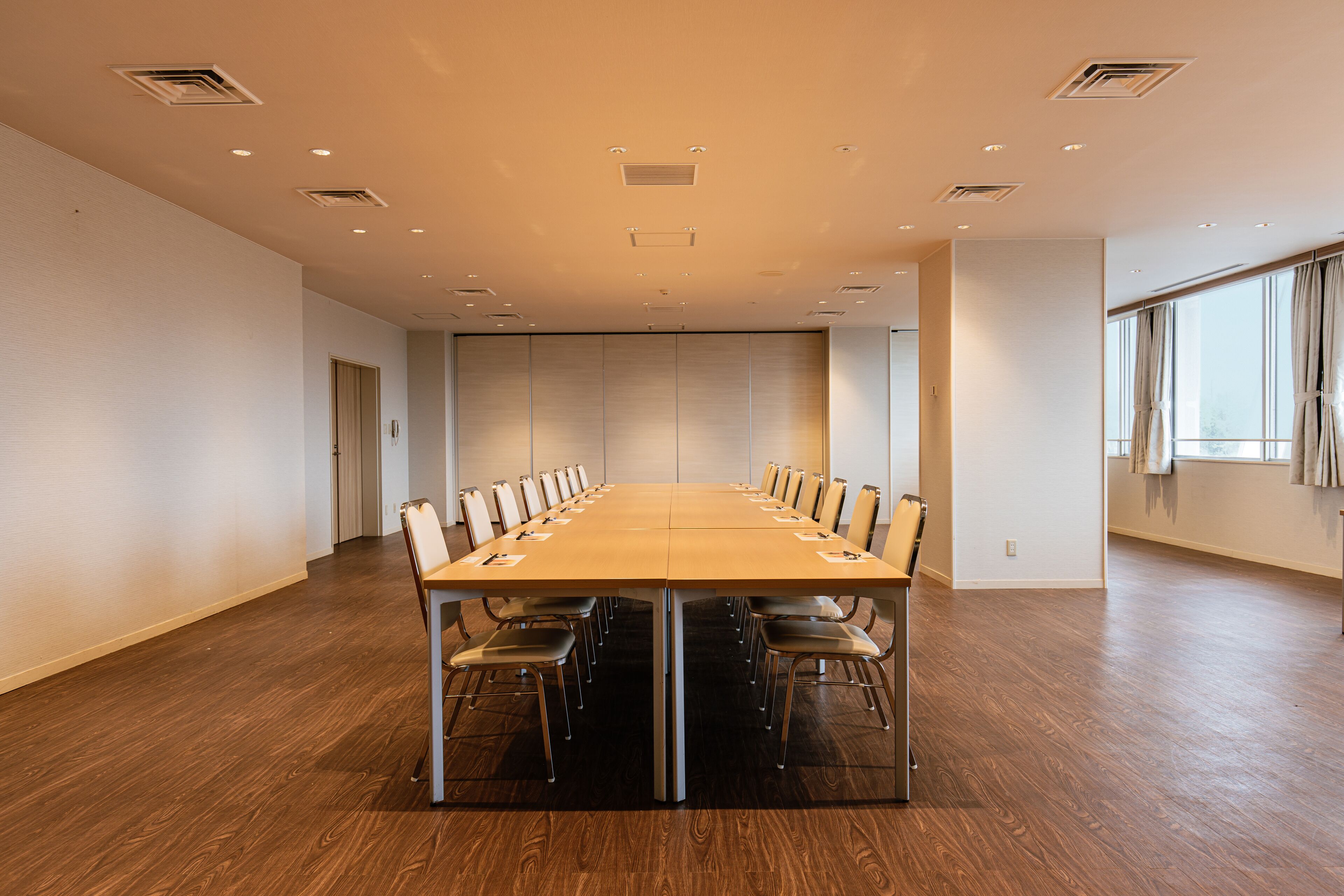 Uma sala de conferências com uma mesa comprida e cadeiras, paredes brancas e um janelão.