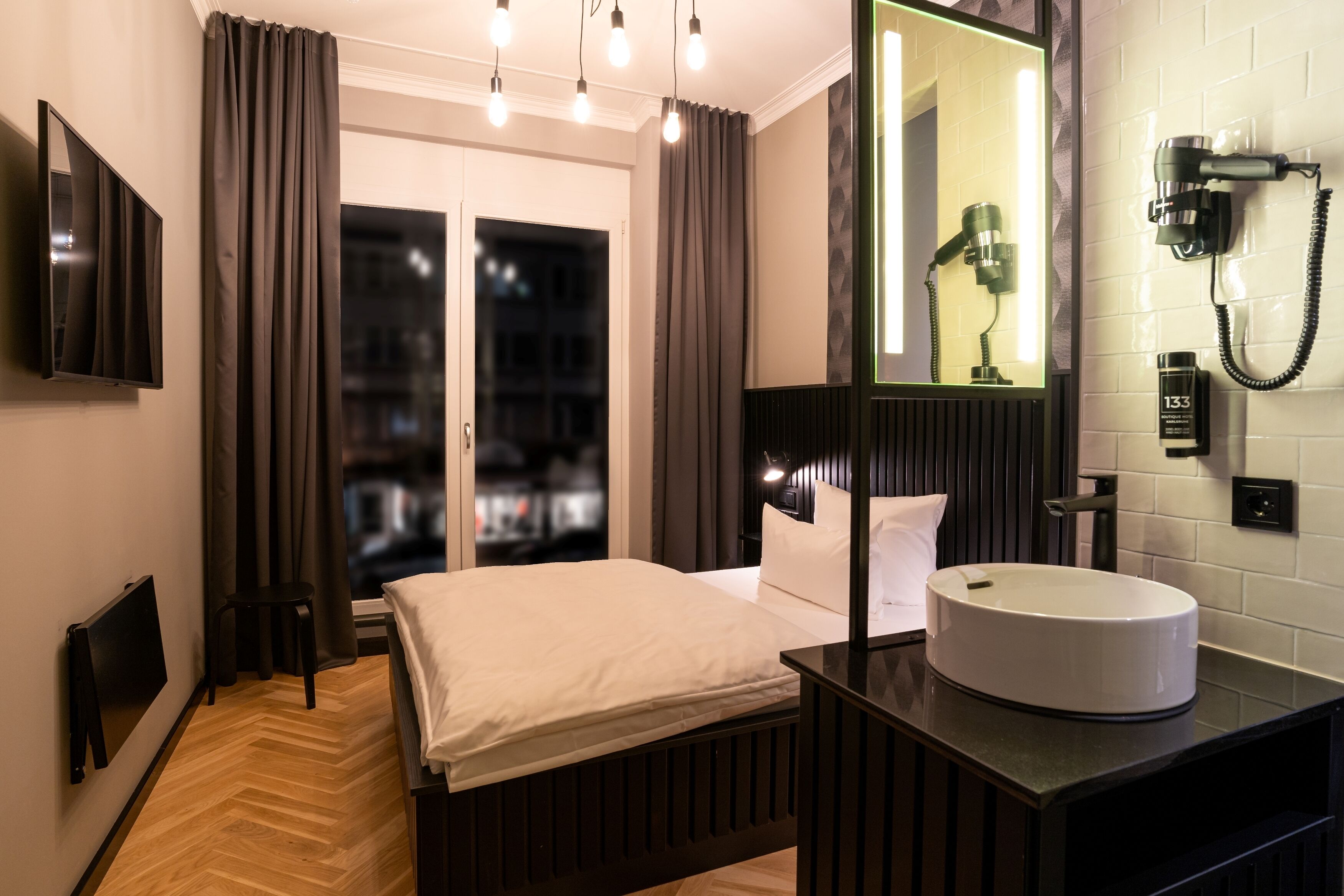 Quarto de hotel moderno com uma cama, um espelho redondo, um secador de cabelo e um telefone.