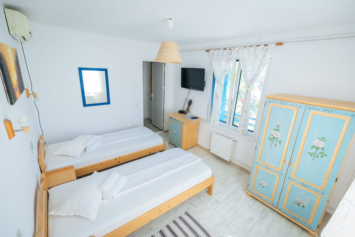 Quarto com duas camas de madeira, televisão, armário e janela com cortinas.