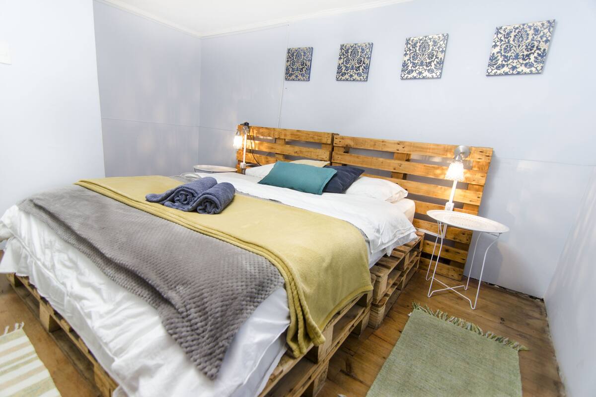 Uma cama com cabeceira de madeira, mesa de cabeceira e luminária na parede.