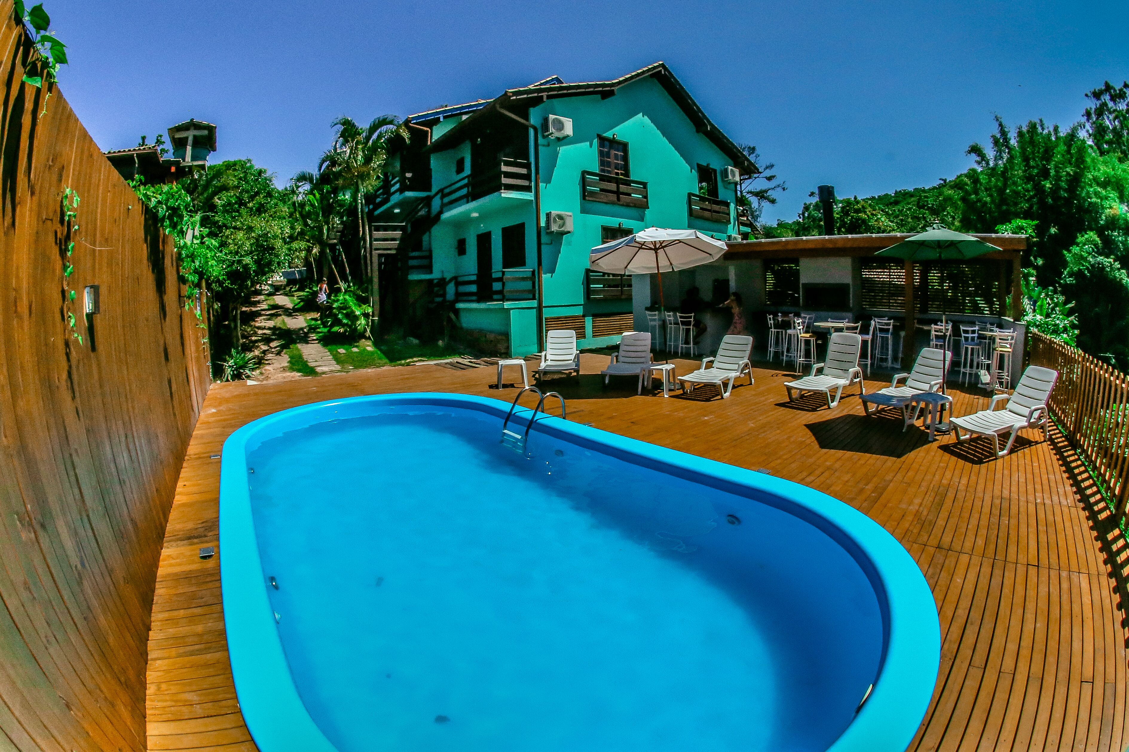 Piscina com deck de madeira, espreguiçadeiras e um edifício ao fundo.