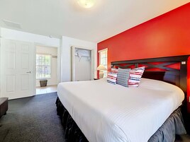 Quarto com uma cama grande, uma parede de destaque vermelha e uma porta branca.