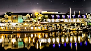 Um hotel à beira-mar com vários edifícios, um barco atracado e águas calmas refletindo as luzes.