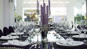 Uma mesa posta para um evento de jantar formal, com vários copos de vinho, pratos e um candelabro com velas.