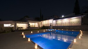 Piscina com borda azulejada, rodeada por um muro baixo e iluminada por velas.