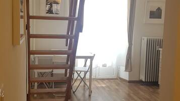 Quarto com escada de madeira, radiador e janela com cortinas.