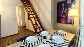 Uma sala de jantar com uma mesa posta para quatro pessoas, uma escadaria e um quadro com vista para a cidade.