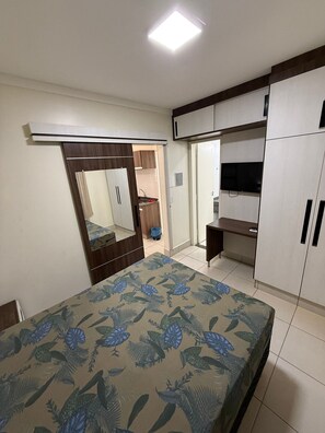 Quarto com cama, guarda-roupa, espelho e televisão.