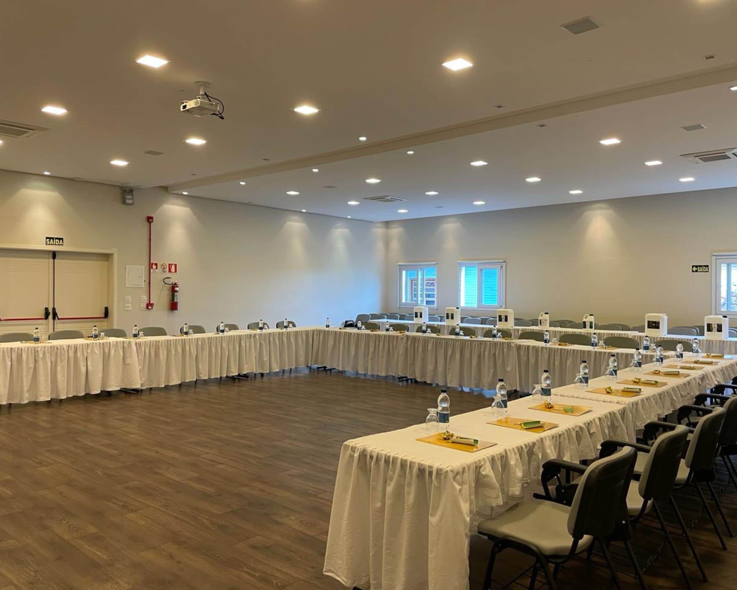 Sala de conferências com várias mesas, cadeiras e um projetor.
