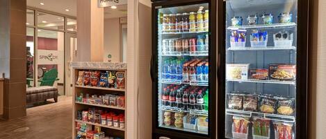 Máquina automática de bebidas e snacks, com sinal indicando que está 'bem gelada'.