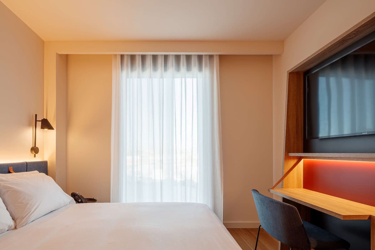 Quarto de hotel moderno com cama, escrivaninha e televisão.