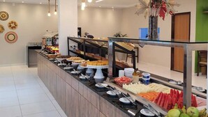 Uma área de buffet com diversos alimentos, incluindo frutas e doces, e um teto decorativo com padrões trançados.