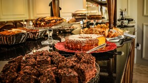 Mesa de buffet com diversos doces, incluindo bolos e brownies, em um ambiente bem iluminado com mobiliário de madeira.