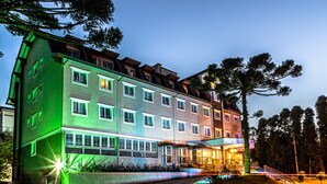Um hotel de vários andares com design moderno, destacando uma entrada imponente, área ajardinada com um pequeno espelho d'água e fachada bem iluminada.
