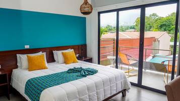 Quarto de hotel com cama grande, varanda com mesa e cadeiras, e vista para edifícios e áreas verdes.