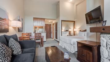 Quarto de hotel com sofá, cama, mesa de centro de madeira, televisão e lareira de pedra.