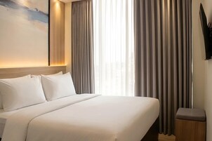 Quarto de hotel com cama, cortinas, televisão presa à parede e um quadro.
