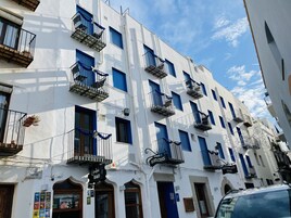 Um edifício branco com persianas azuis e varandas, um letreiro com a inscrição 'Calle Mayor' e um letreiro de 'Bar'.