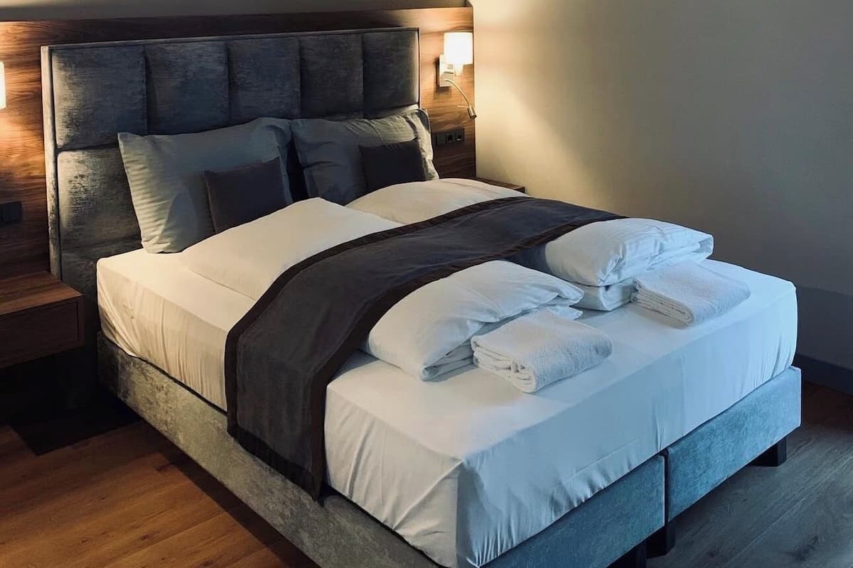 Cama bem arrumada com cabeceira, mesa de cabeceira e luminária fixada na parede.