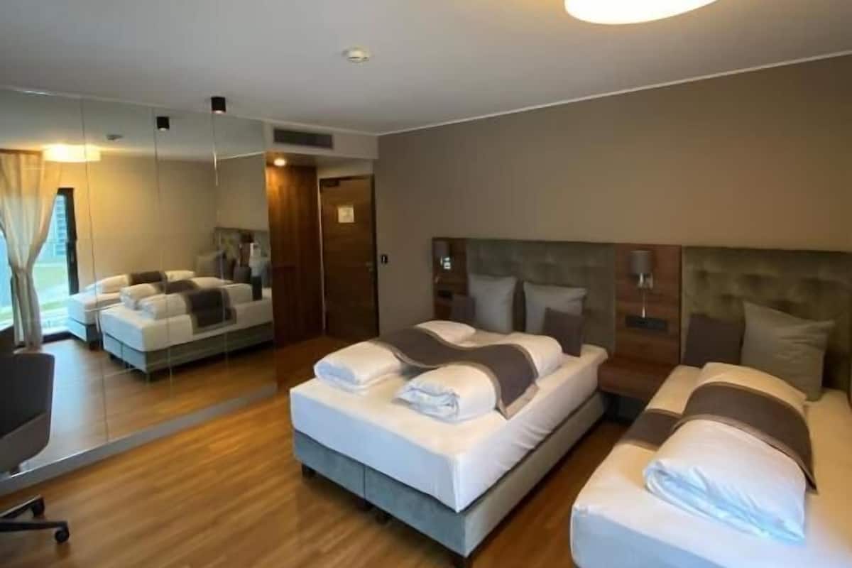 Quarto de hotel moderno com duas camas, um espelho grande e piso de madeira.