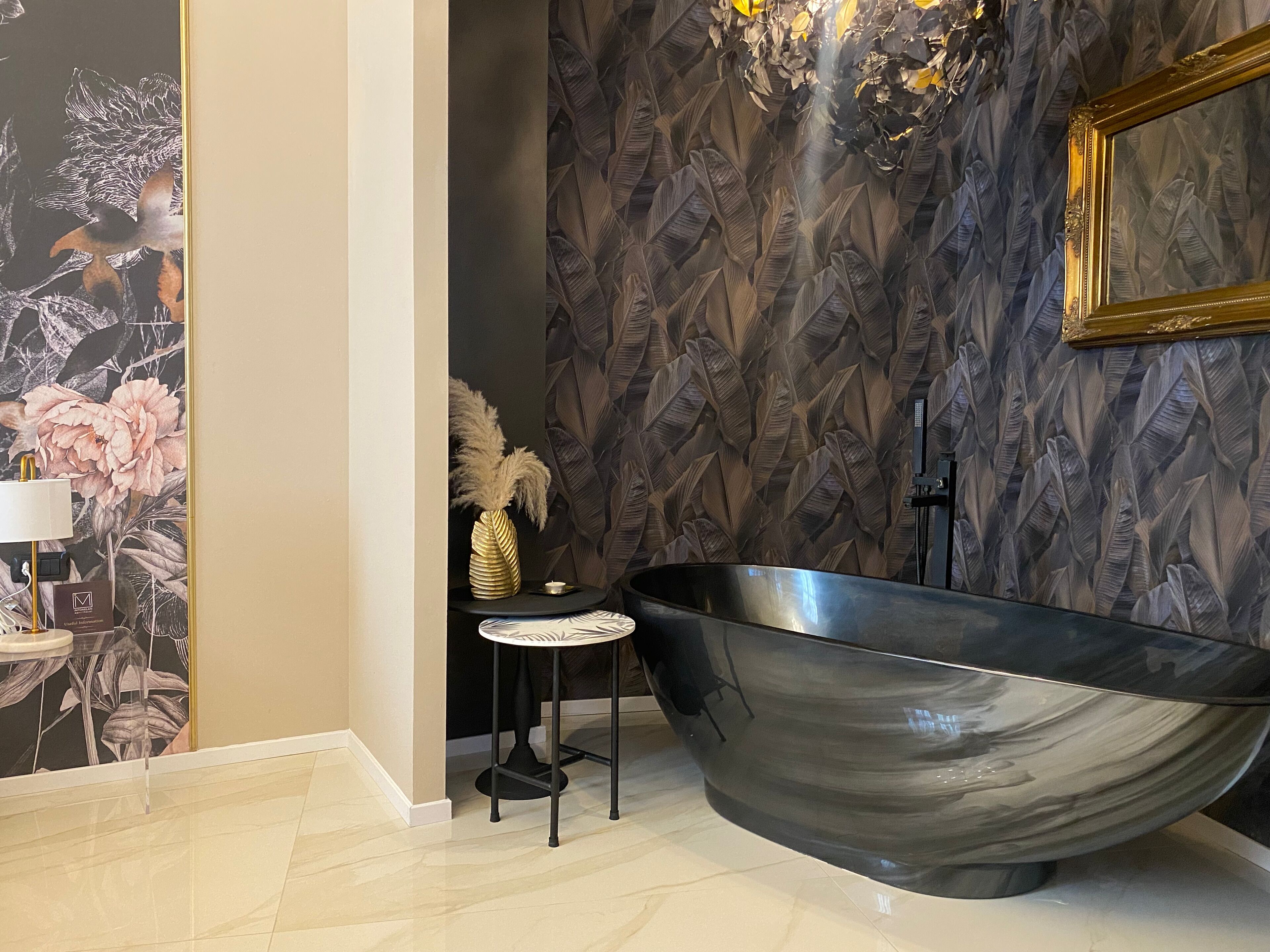 Um banheiro moderno com uma banheira de pedestal, uma mesinha lateral com abajur e um vaso decorativo.