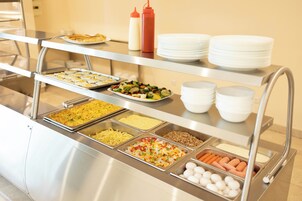 Buffet com diversas opções de comida, incluindo ovos, cachorros-quentes e saladas.