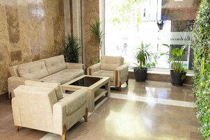 Um hall com sofá bege, mesa de centro e plantas em vasos.