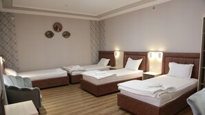Quarto de hotel com quatro camas de solteiro, um sofá e uma escrivaninha.