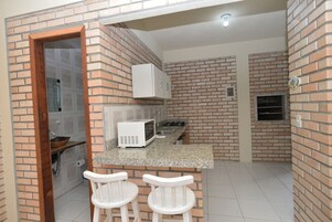 Cozinha compacta com painel de parede em tijolo, micro-ondas, fogão a gás e dois bancos de bar brancos.