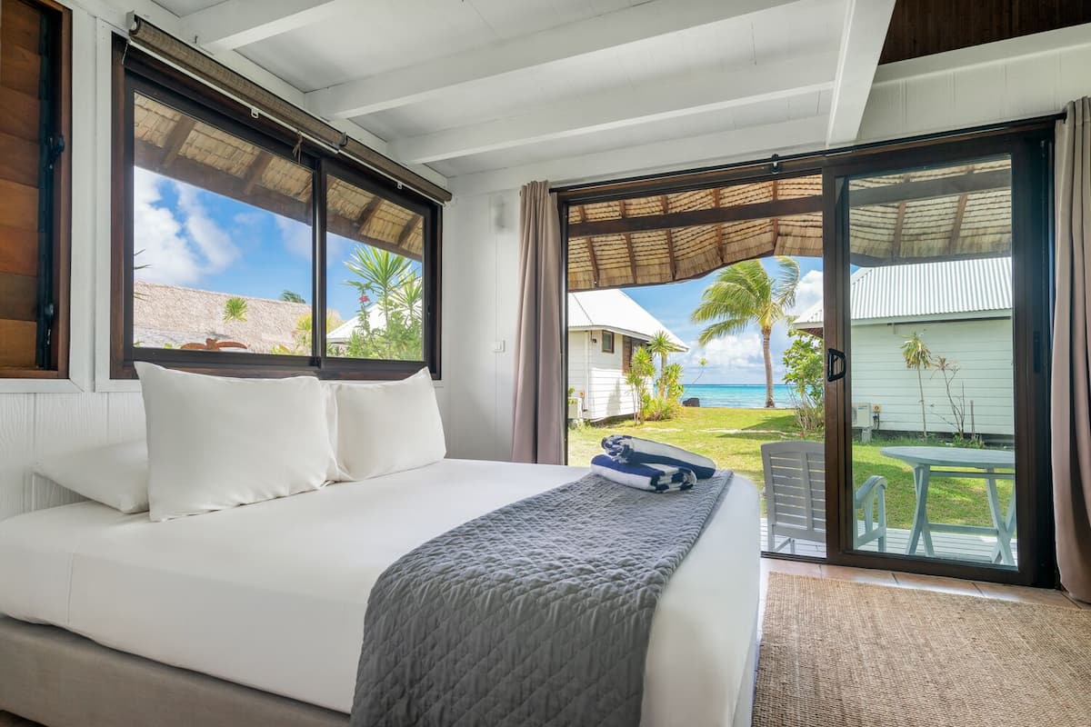 Quarto com cama grande, vista para o oceano e varanda com mesa e cadeiras.