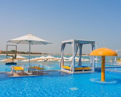 Uma área de piscina com espreguiçadeiras e guarda-sóis, um elemento aquático e vista para a praia.