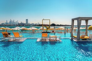 Piscina com espreguiçadeiras e guarda-sóis, com um horizonte urbano ao fundo e céu azul.